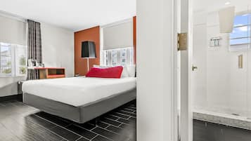 Quarto de hotel moderno com uma cama grande, mesa de cabeceira, luminária e vista para a cidade pela janela.