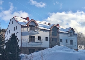 Um edifício de vários andares com varandas, fachada de pedra e paisagem coberta de neve.
