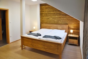Quarto com cama de madeira, duas mesas de cabeceira com abajures e teto inclinado revestido em madeira.