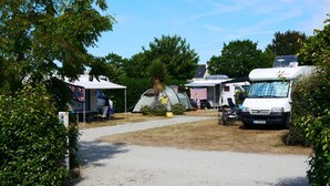 Um camping com veículos recreativos e tendas, um caminho de cascalho e vegetação ao redor.