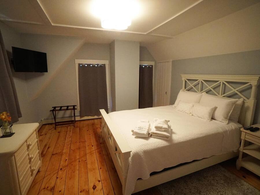 Quarto com uma cama grande, cômoda, mesa de cabeceira, televisão na parede e piso de madeira.