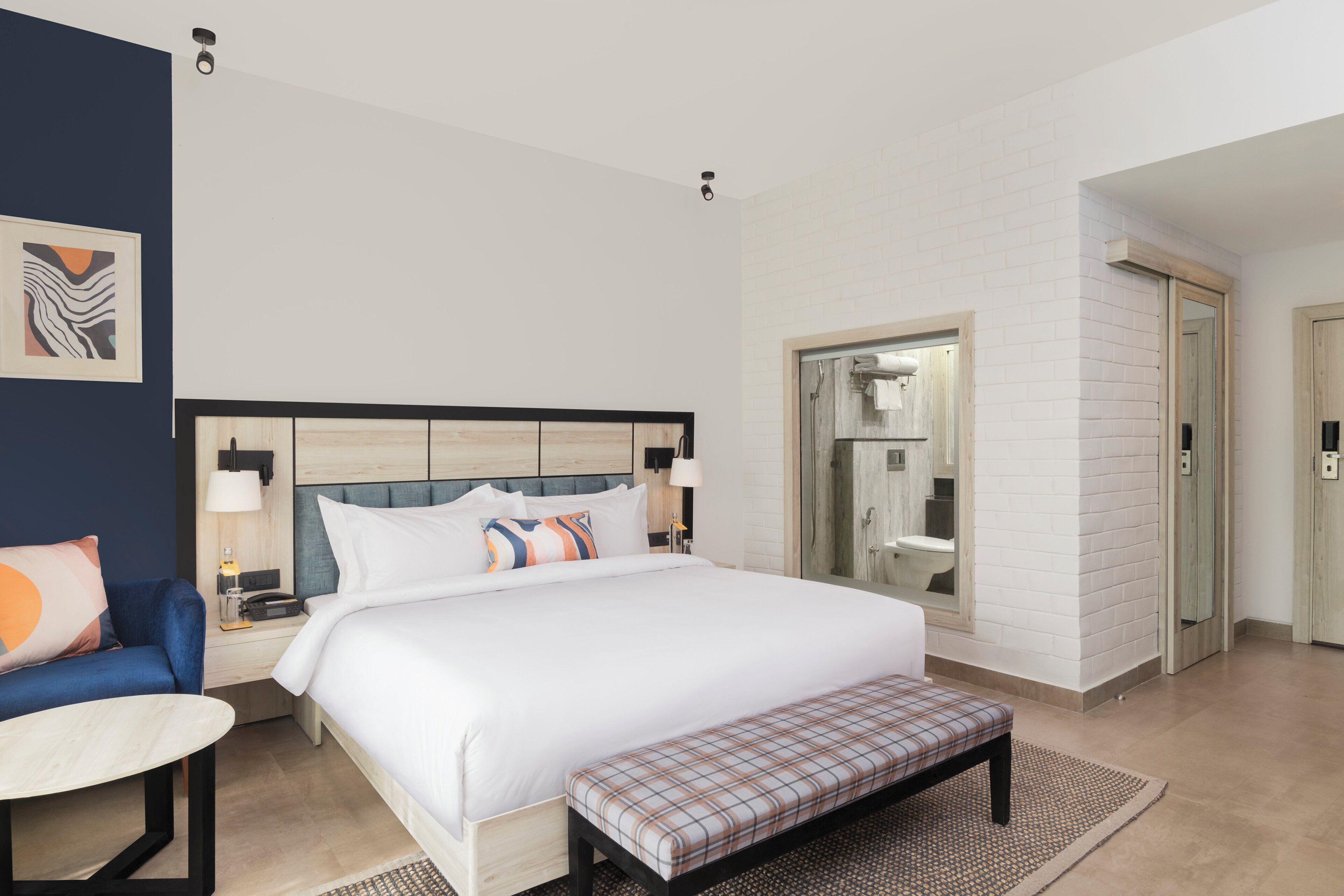 Quarto de hotel com cama, mesa de cabeceira, cadeira e banheiro com chuveiro e vaso sanitário.