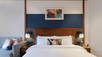 Quarto de hotel com uma cama, duas mesas de cabeceira, uma luminária, uma obra de arte na parede e um sofá.