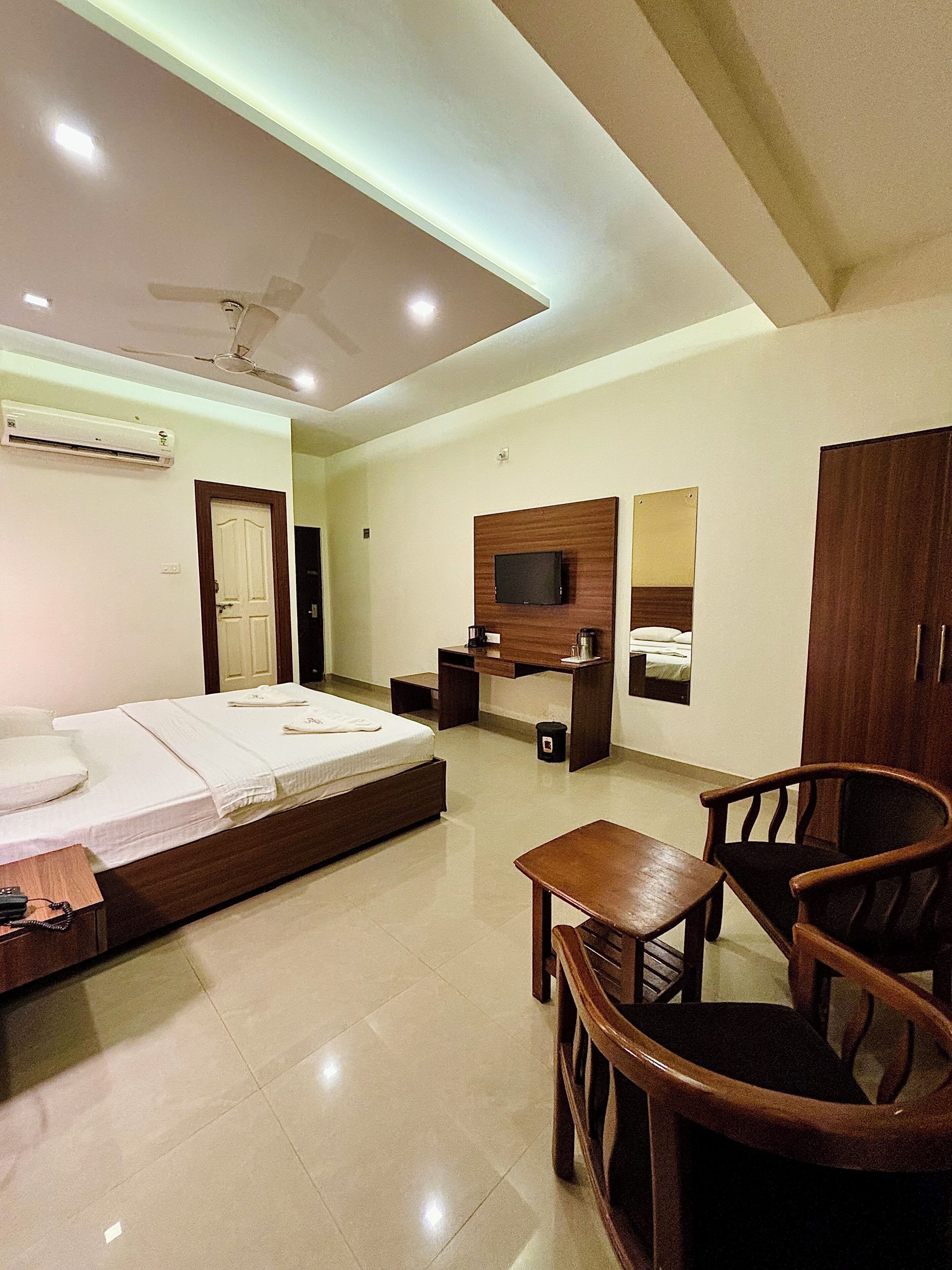 Quarto de hotel com cama, escrivaninha, cadeira, televisão e ar condicionado.