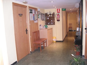 Corredor com portas de madeira, uma cadeira de madeira, extintor de incêndio e lixeira.