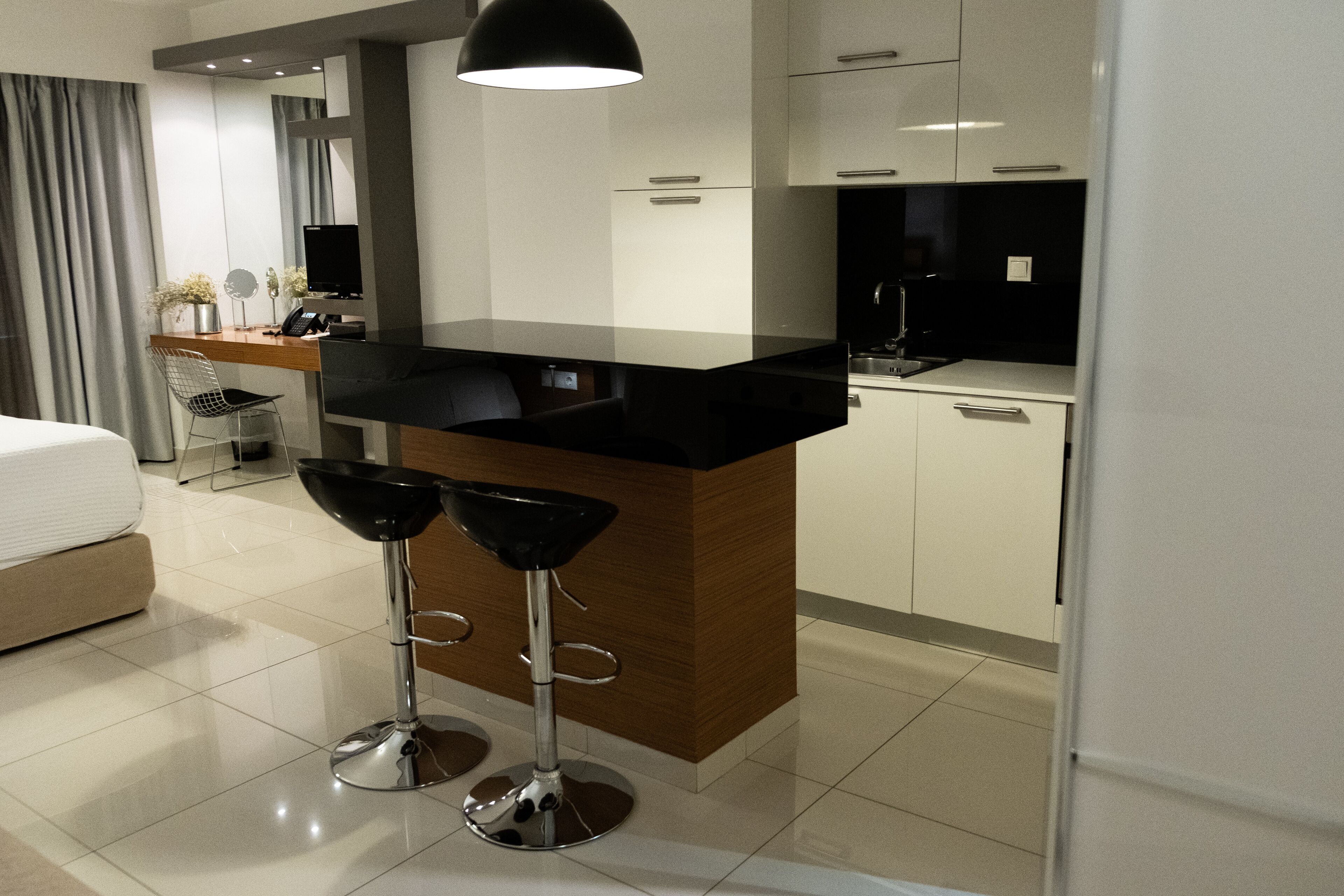 Quarto de hotel moderno com cozinha, mesa de jantar e dois banquetes, cama e um espelho grande.