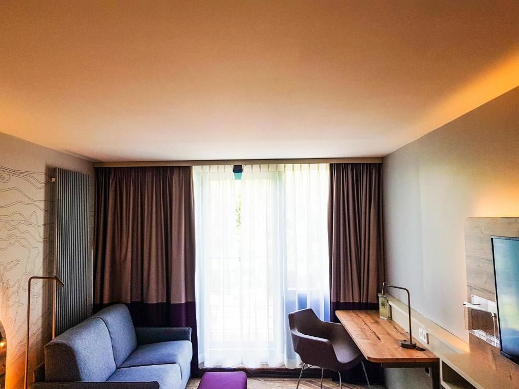 Quarto de hotel com sofá, mesa pequena, cadeira e televisão.