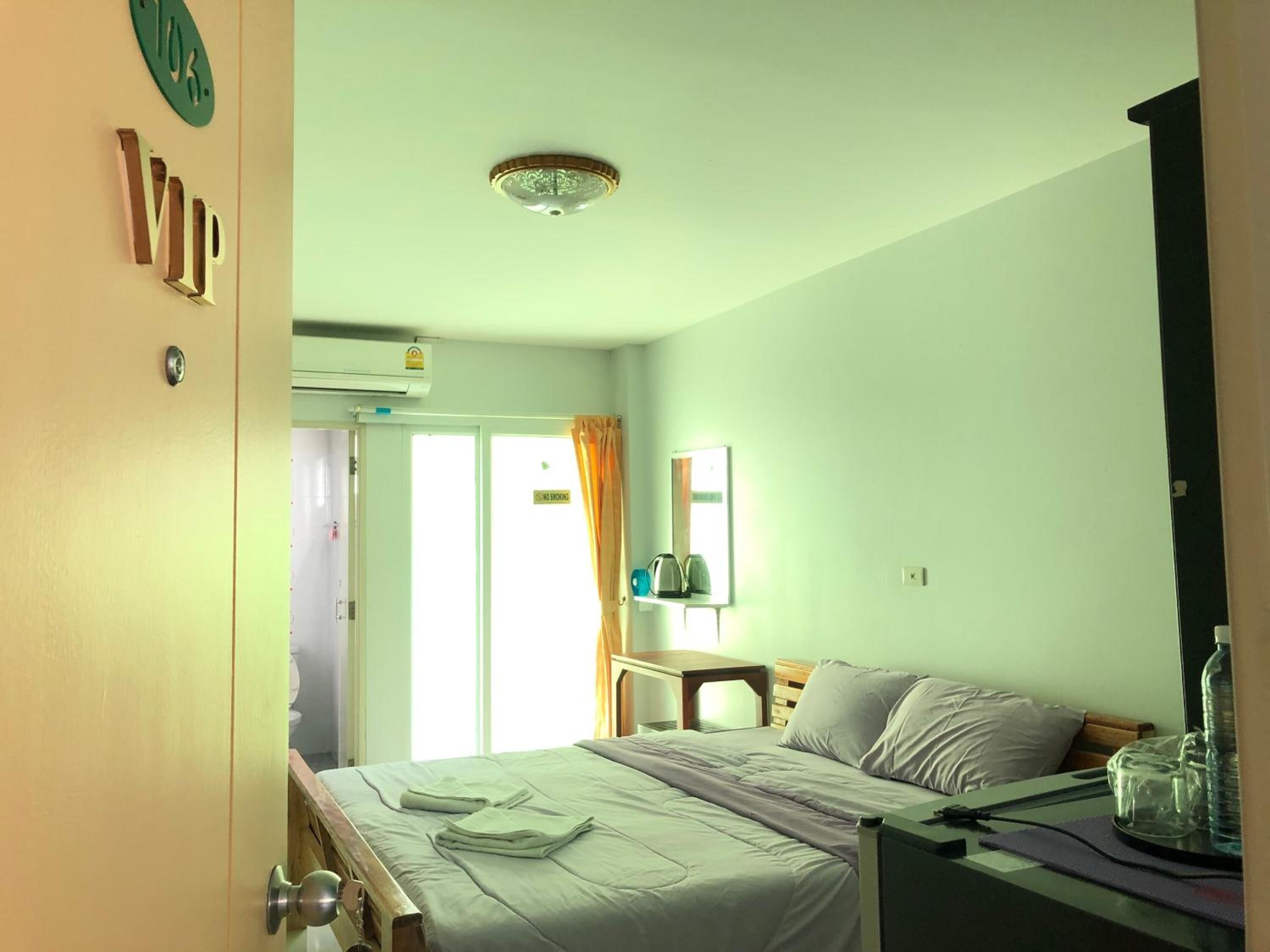 Quarto com cama, mesa de cabeceira, espelho e janela com cortinas.