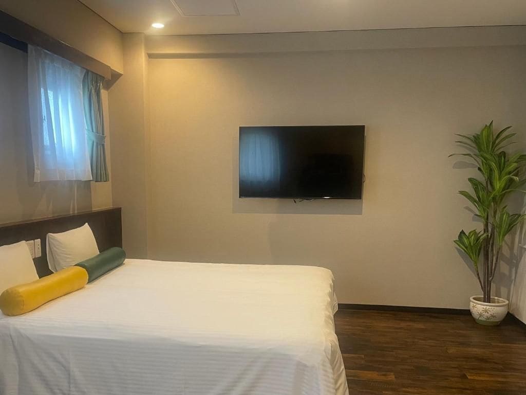 Quarto de hotel com cama, televisão de tela plana na parede e planta em vaso.