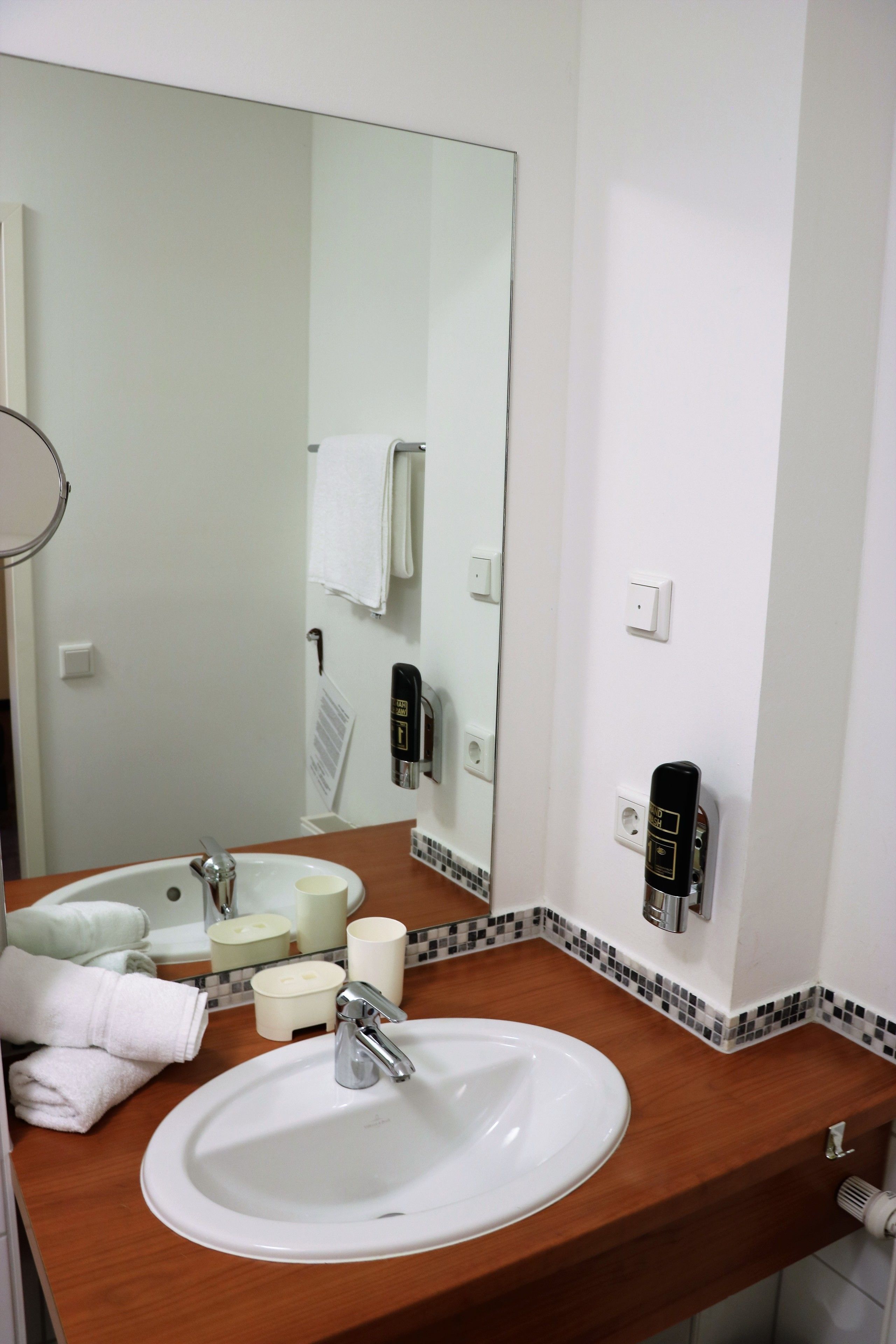Casa de banho com lavatório branco, espelho e suporte de toalhas.