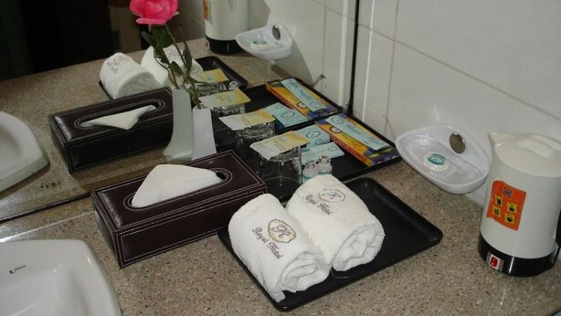 Casa de banho de hotel com artigos de higiene pessoal, toalhas, máquina de café e um vaso com flores.