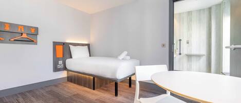 Quarto de hotel moderno com uma cama, mesa de cabeceira e uma mesa de jantar redonda com cadeiras.