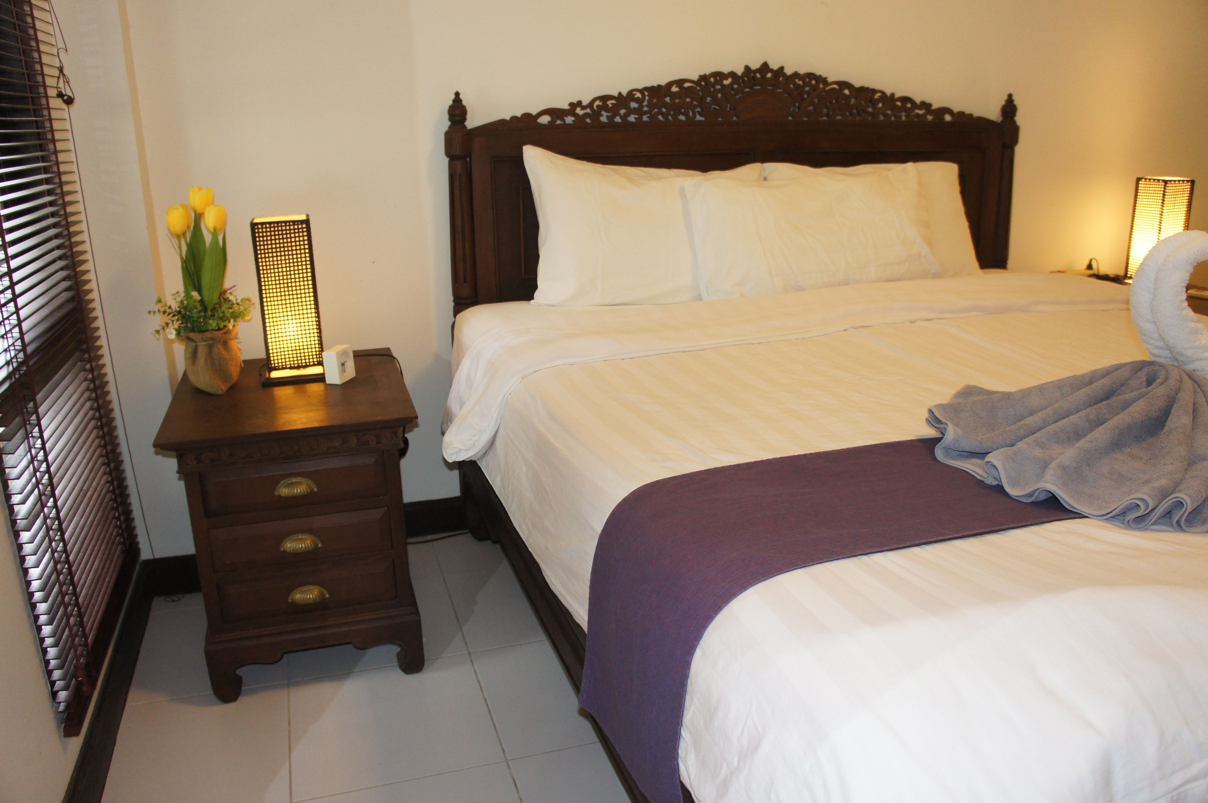 Uma cama de casal com cabeceira de madeira, uma mesinha de cabeceira com um vaso de flores e um abajur.