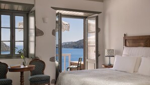 Quarto com cama, uma cadeira, uma mesa e vista para o mar.