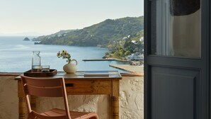 Vista de uma varanda com uma mesa de madeira, uma cadeira, um vaso com flores e um jarro de vidro.