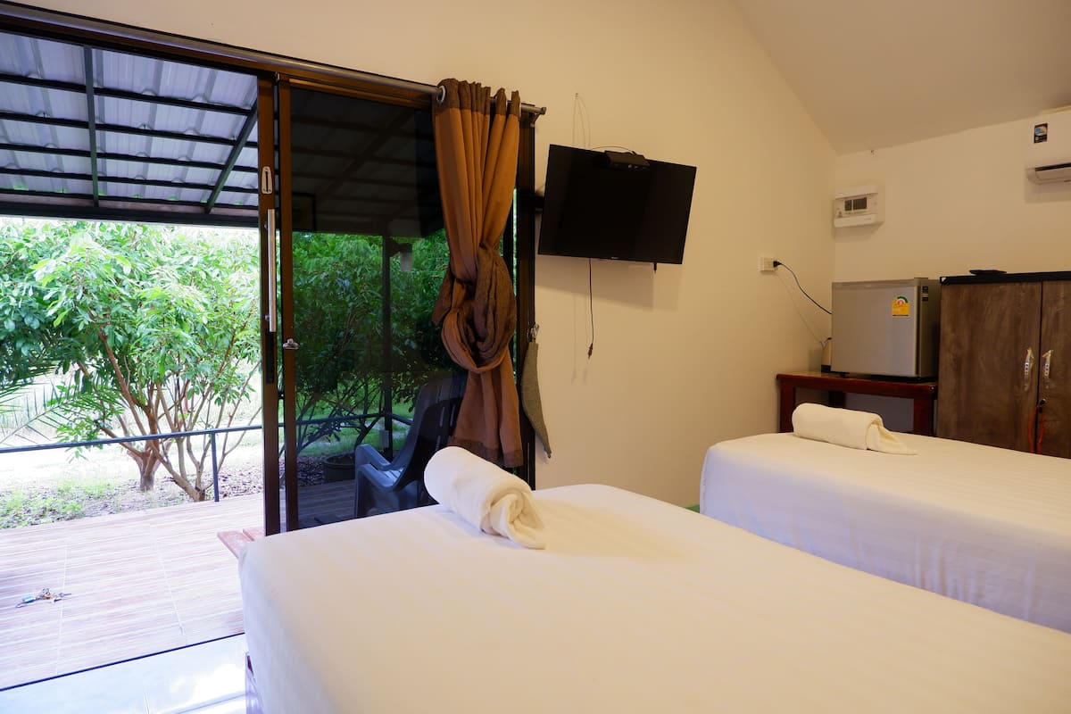 Quarto de hotel com duas camas, televisão e vista para o verde lá fora.