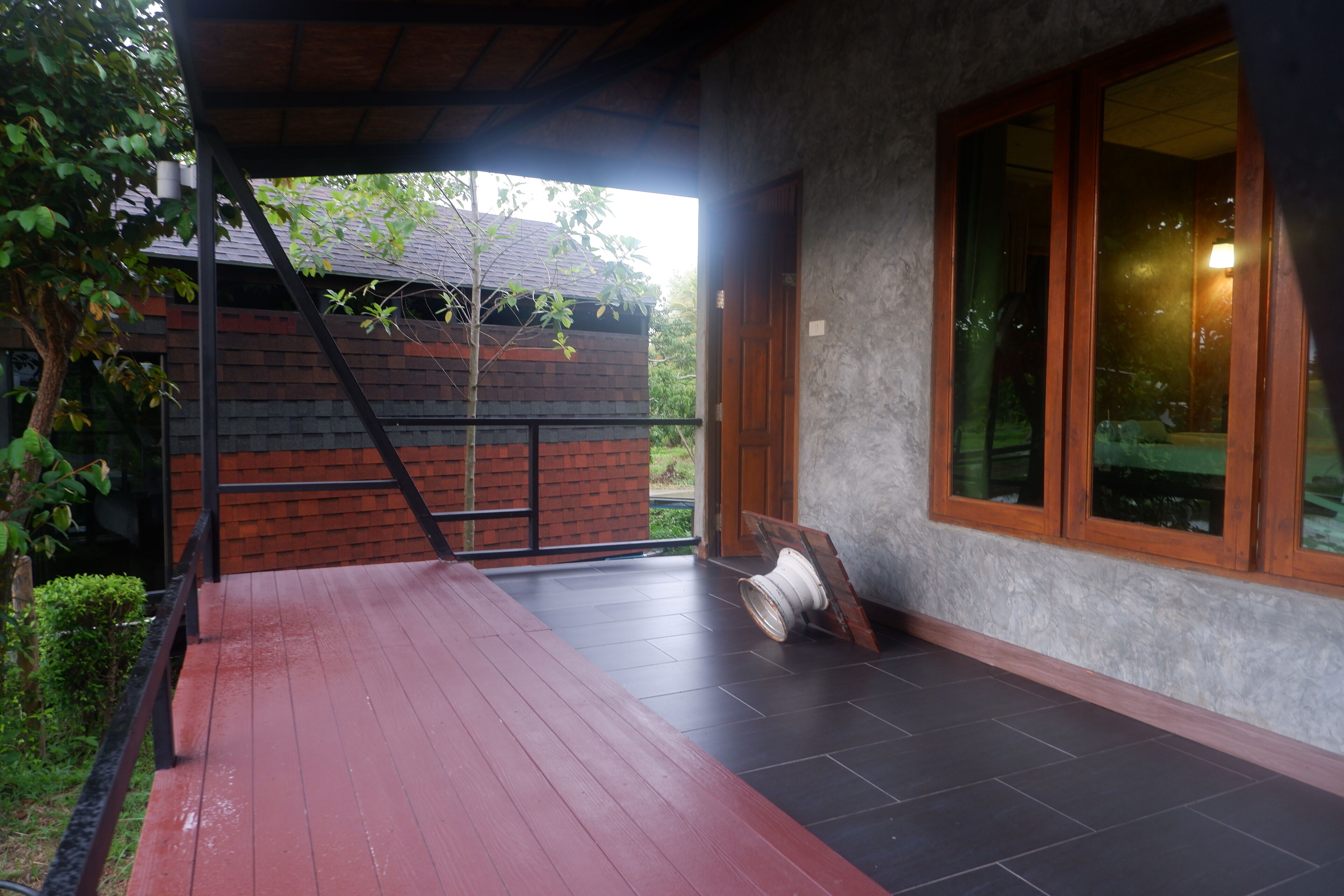 Um espaço ao ar livre coberto com um banco de madeira vermelho, uma parede de tijolos e uma janela com molduras de madeira.