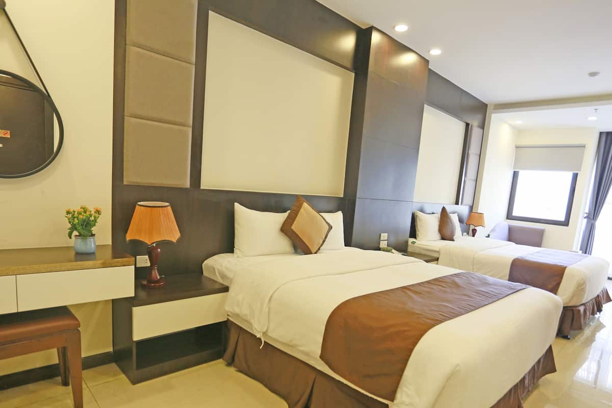 Quarto de hotel com duas camas, uma escrivaninha, um abajur e um espelho.