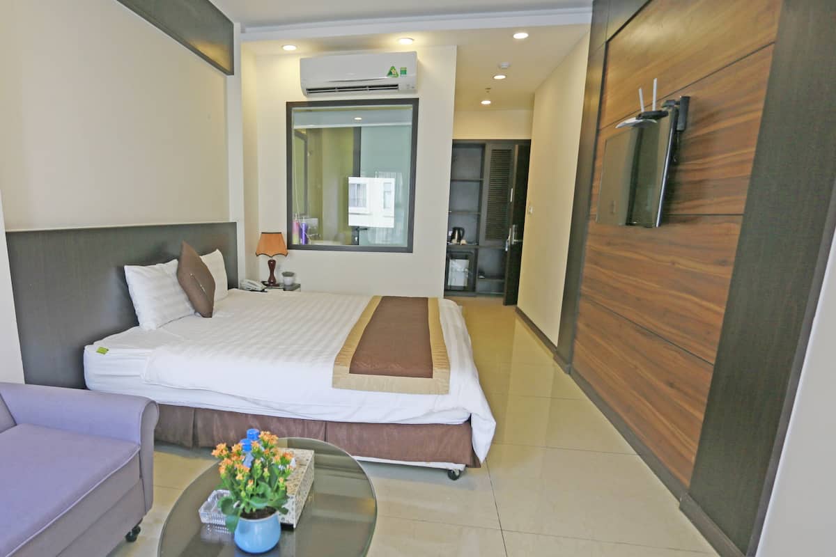 Quarto de hotel com cama, sofá, mesinha com planta e espelho.