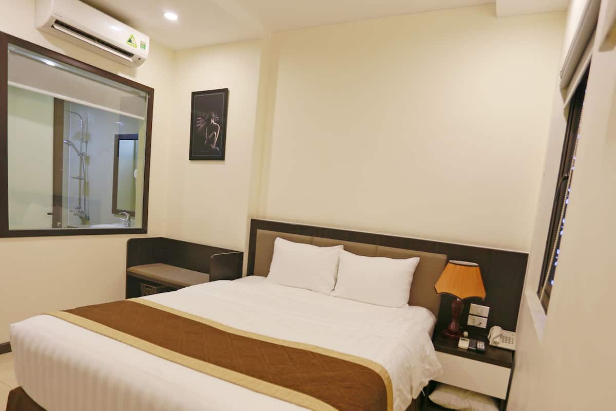 Quarto de hotel com cama, mesa de cabeceira, abajur e espelho.