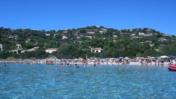 Uma praia com águas azul-claras e uma encosta ao fundo.