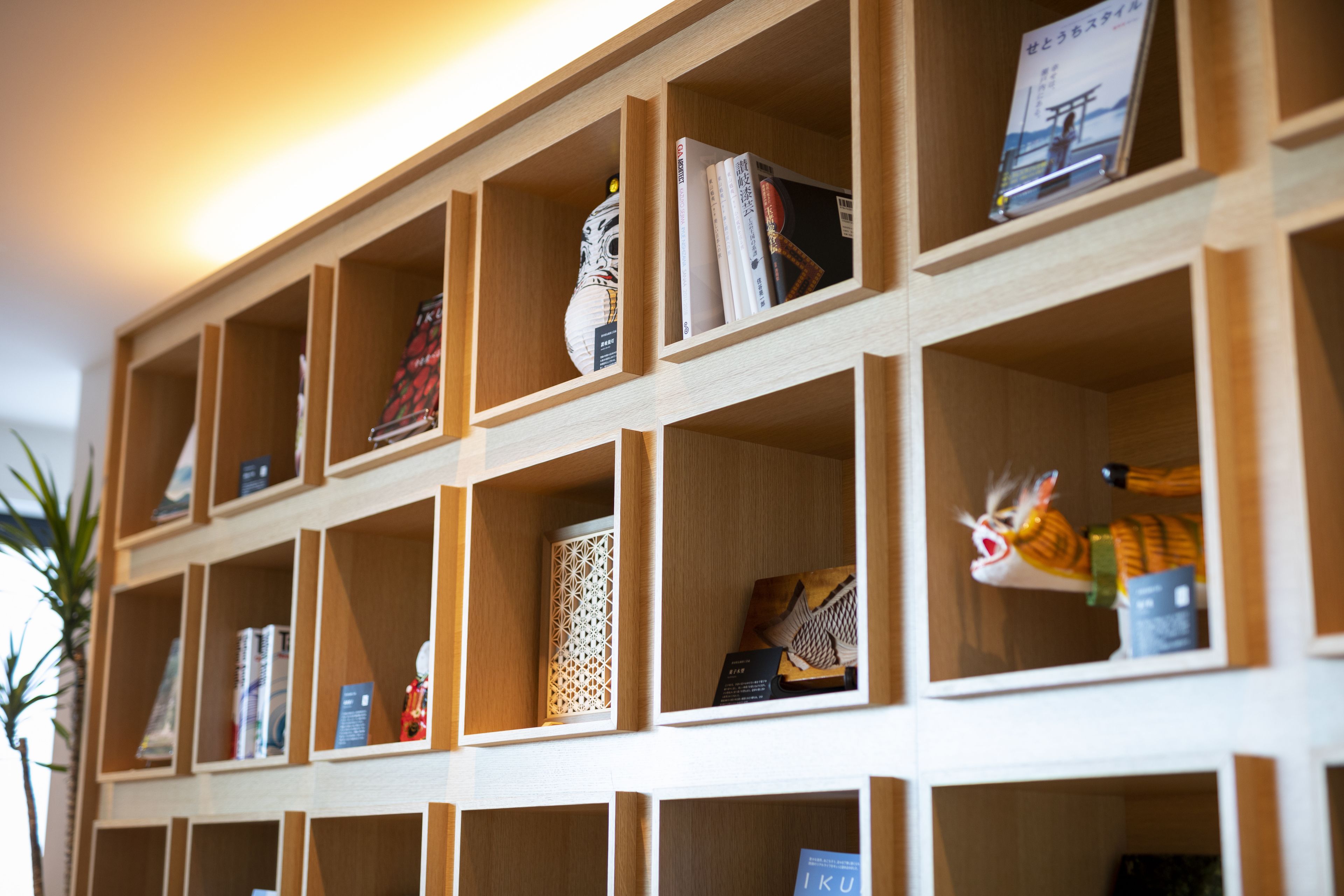 Uma estante de madeira com vários compartimentos, cada um contendo livros, objetos decorativos e uma pequena planta.