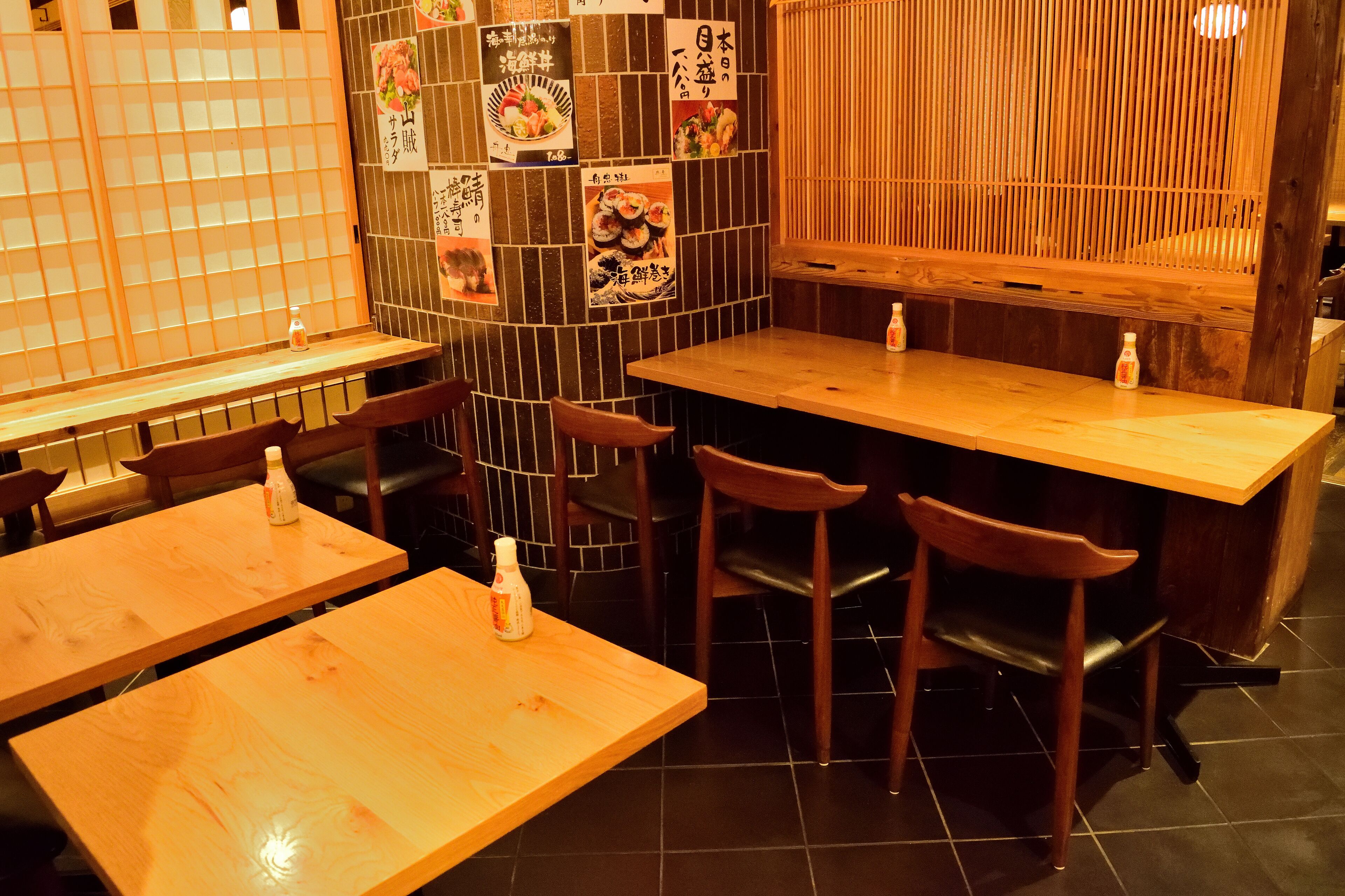 Interior de restaurante com mesas e cadeiras de madeira, parede revestida com cartazes de menu, e divisória de madeira.
