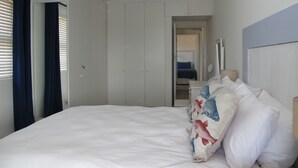 Quarto com cama, ventoinha no teto, guarda-roupa e porta que dá para outro cômodo.