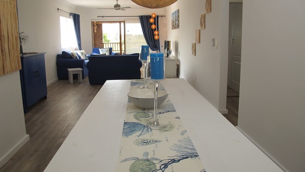 Uma sala de estar moderna com um sofá, uma mesa de jantar com um jogo americano decorativo e um ventilador de teto.