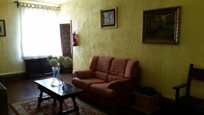 Uma sala de estar com um sofá, uma mesinha com um vaso e uma janela com cortinas.