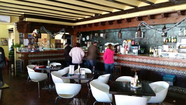 Uma área de bar com balcão, cadeiras brancas e teto de madeira rústica.