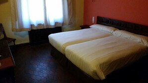 Quarto de hotel com duas camas, uma cabeceira de madeira, uma cadeira de madeira e piso de azulejos.