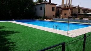 Piscina retangular com duas plataformas de mergulho, rodeada por um gramado verde e uma cerca.
