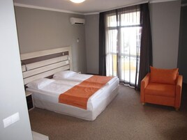 Quarto de hotel com uma cama grande, uma cadeira, janela com cortinas e ar condicionado.