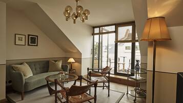 Uma sala de estar moderna com um sofá verde, cadeiras de madeira, uma mesa de centro de vidro, um candelabro e um abajur.