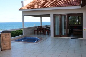 Uma área externa coberta com piscina, assentos e vista para o oceano.