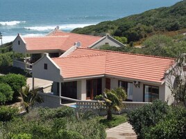 Uma casa costeira com telhado de telhas vermelhas, piscina e vista para o oceano.