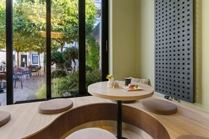 Um interior moderno com uma mesa redonda, assentos acolchoados e vista para um jardim exterior através de amplas janelas.