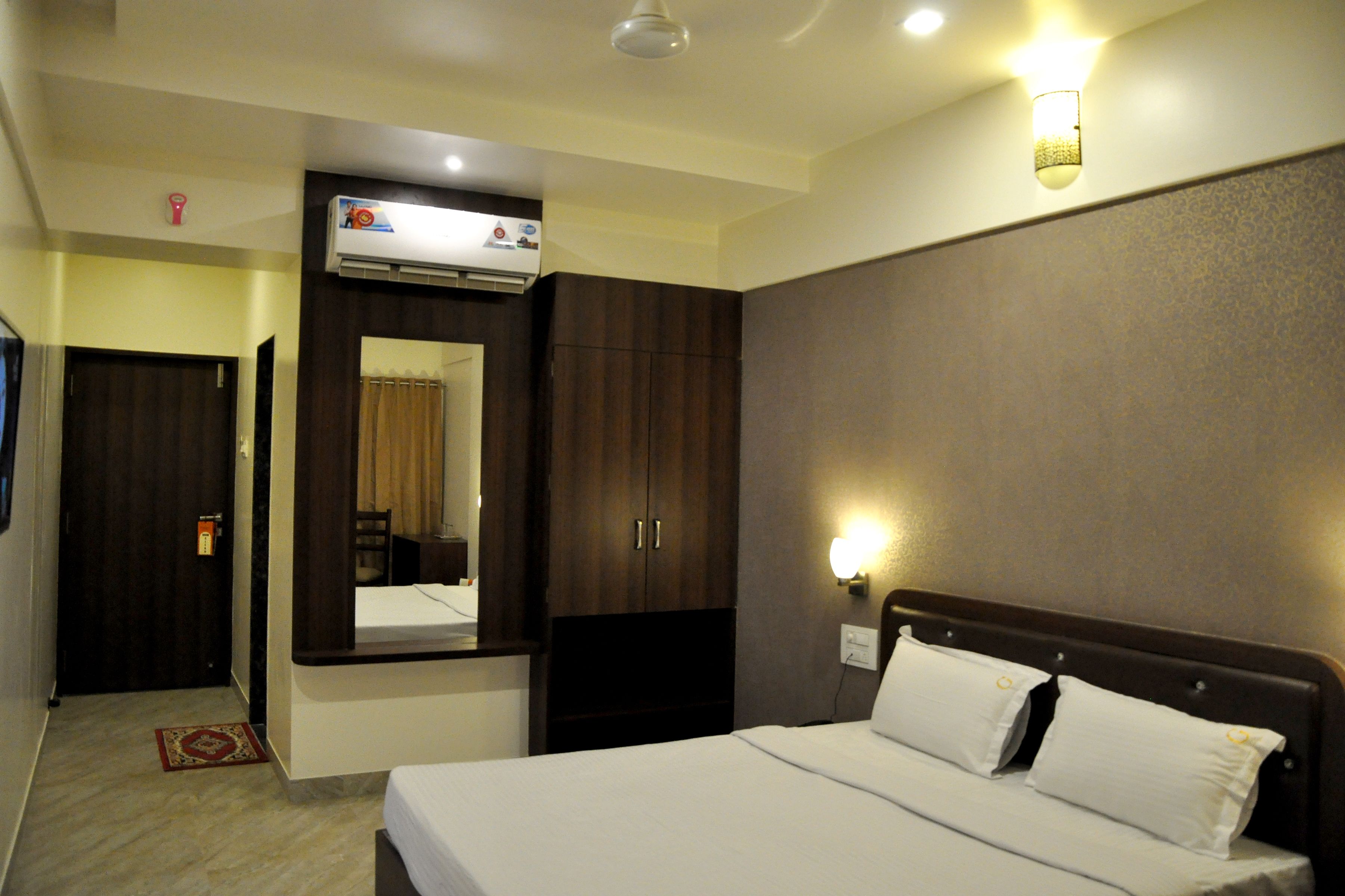 Quarto de hotel com cama, guarda-roupa, espelho, ar condicionado e luminária.