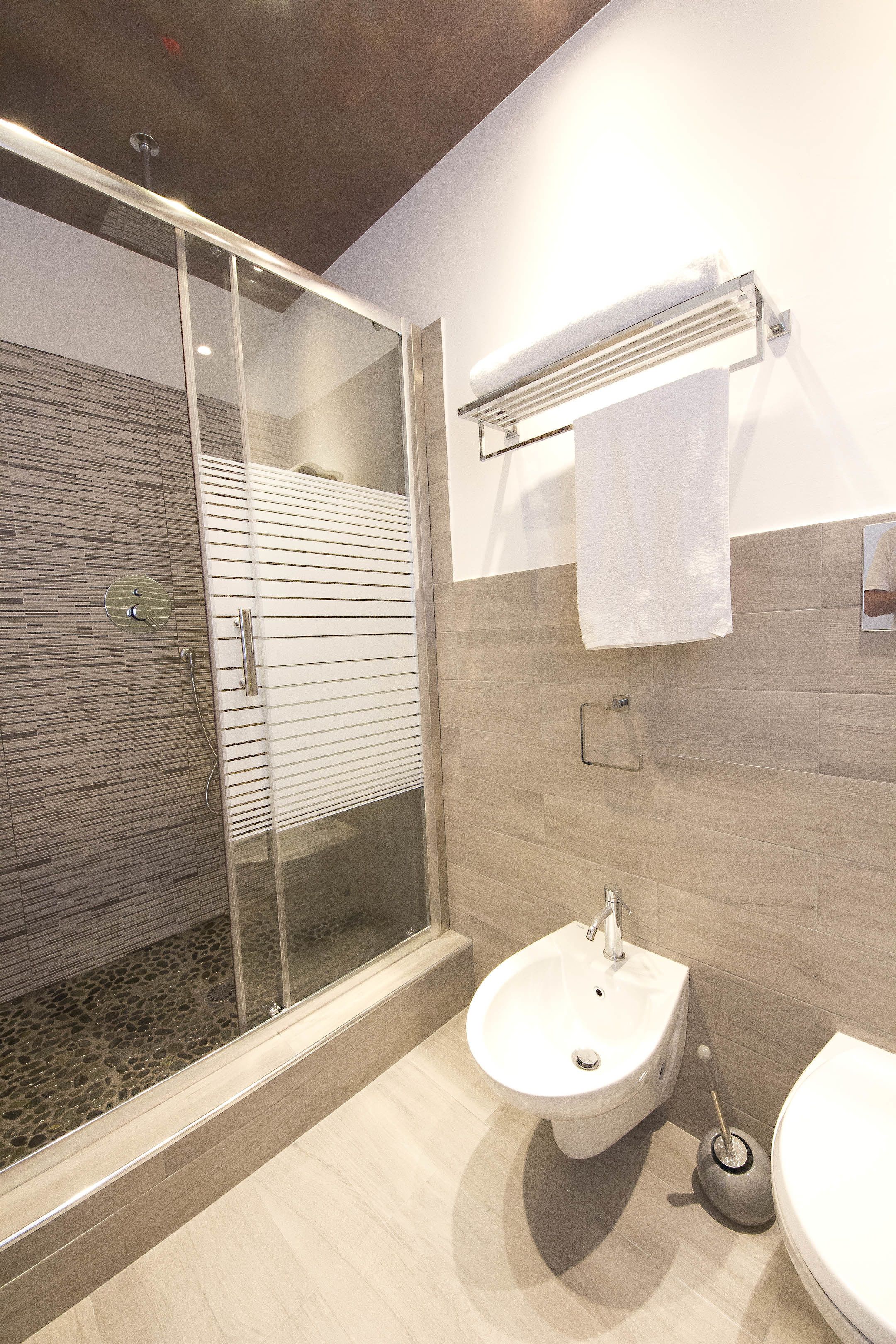 Um banheiro moderno com box de vidro, bidê e porta-toalhas.