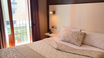 Quarto de hotel com uma cama grande, mesa de cabeceira, luminária na parede e vista para uma varanda.