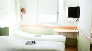 Quarto de hotel com duas camas, televisão, secretária pequena e janela.
