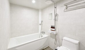 Um banheiro moderno com banheira branca, chuveiro e vaso sanitário. Há uma prateleira com produtos de higiene pessoal e um porta-toalhas na parede.
