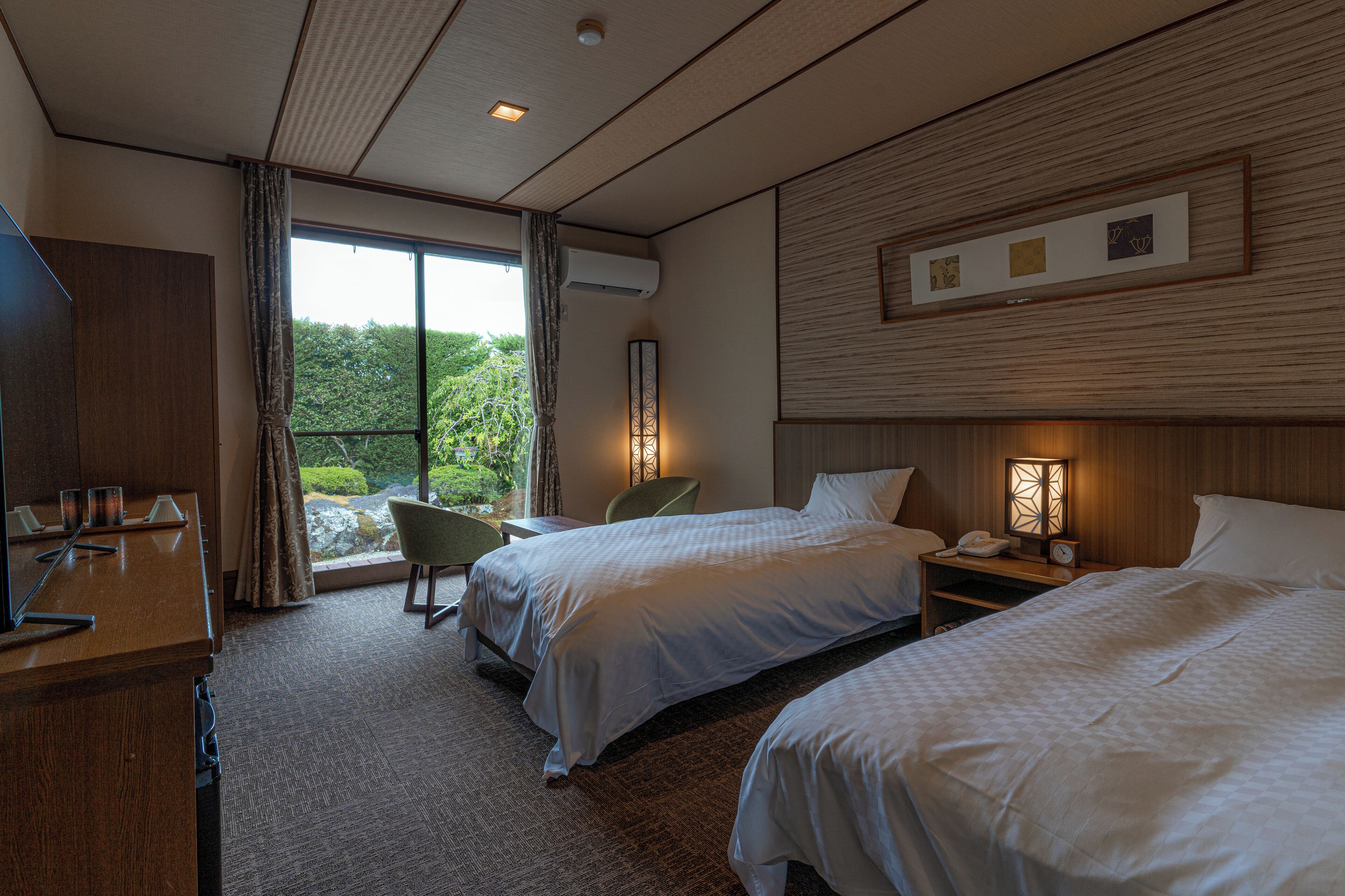 Quarto de hotel com duas camas, uma escrivaninha, uma cadeira e uma televisão.