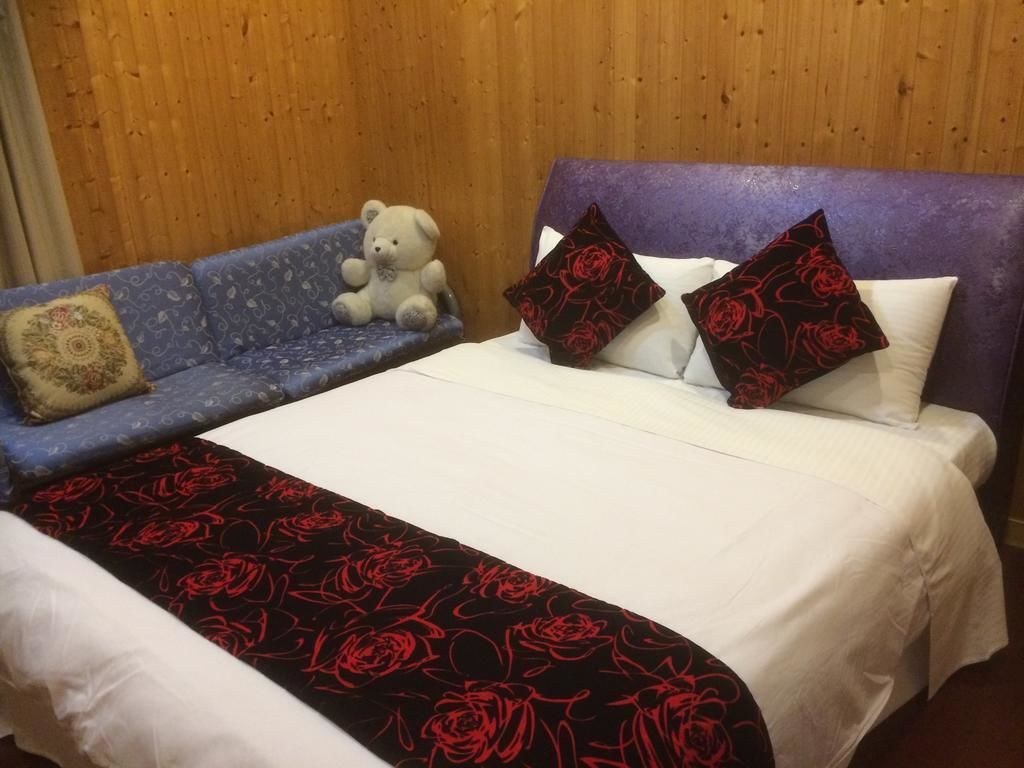 Uma cama com roupa de cama branca e um cobertor estampado com rosas pretas e vermelhas. Há um sofá azul com um ursinho de pelúcia e uma almofada decorativa.