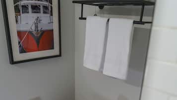 Casa de banho com sanita, um quadro na parede, uma pilha de toalhas brancas e rolo de papel higiénico.