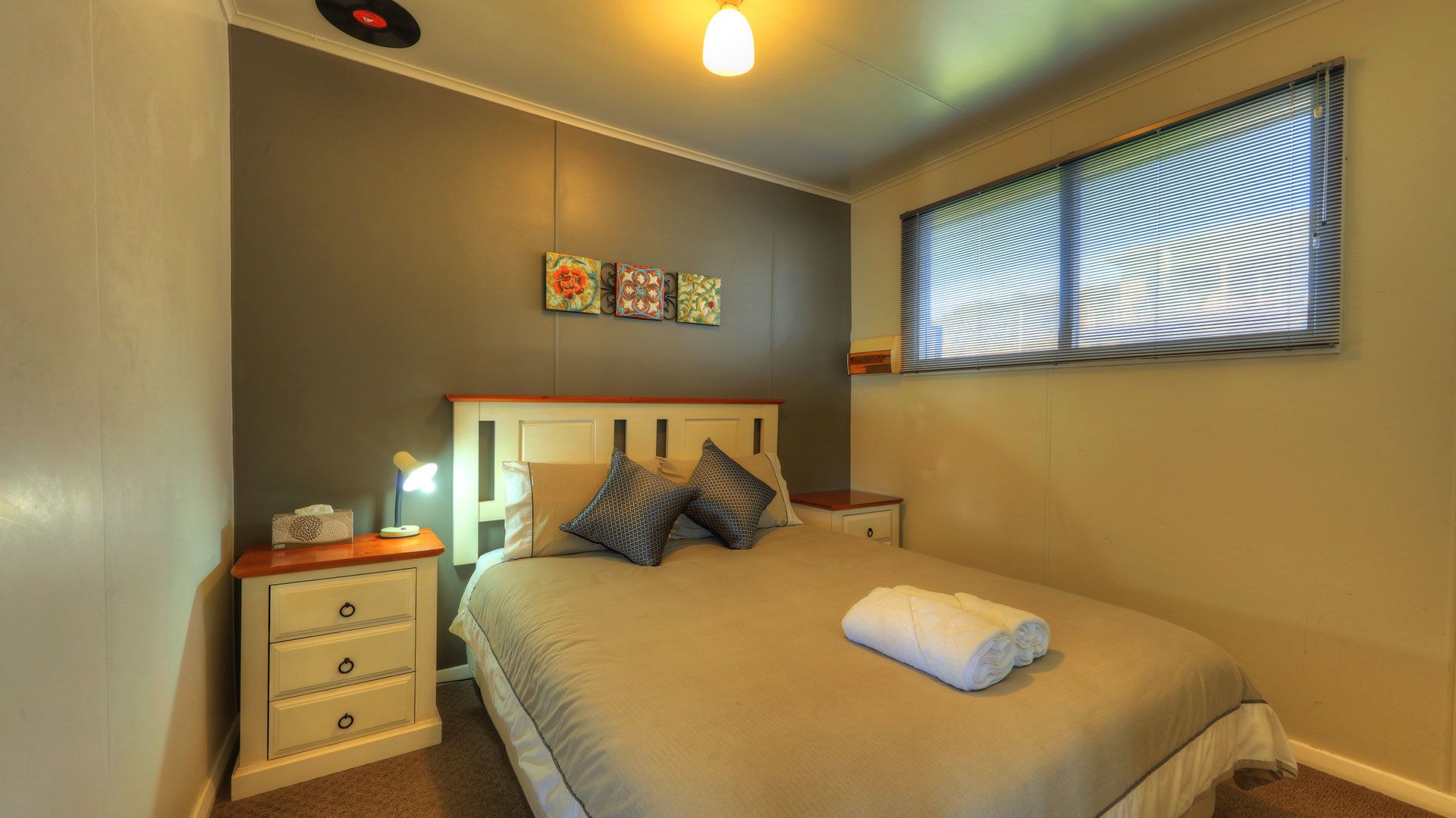 Quarto com cama, mesas de cabeceira, abajur e janela com persianas.