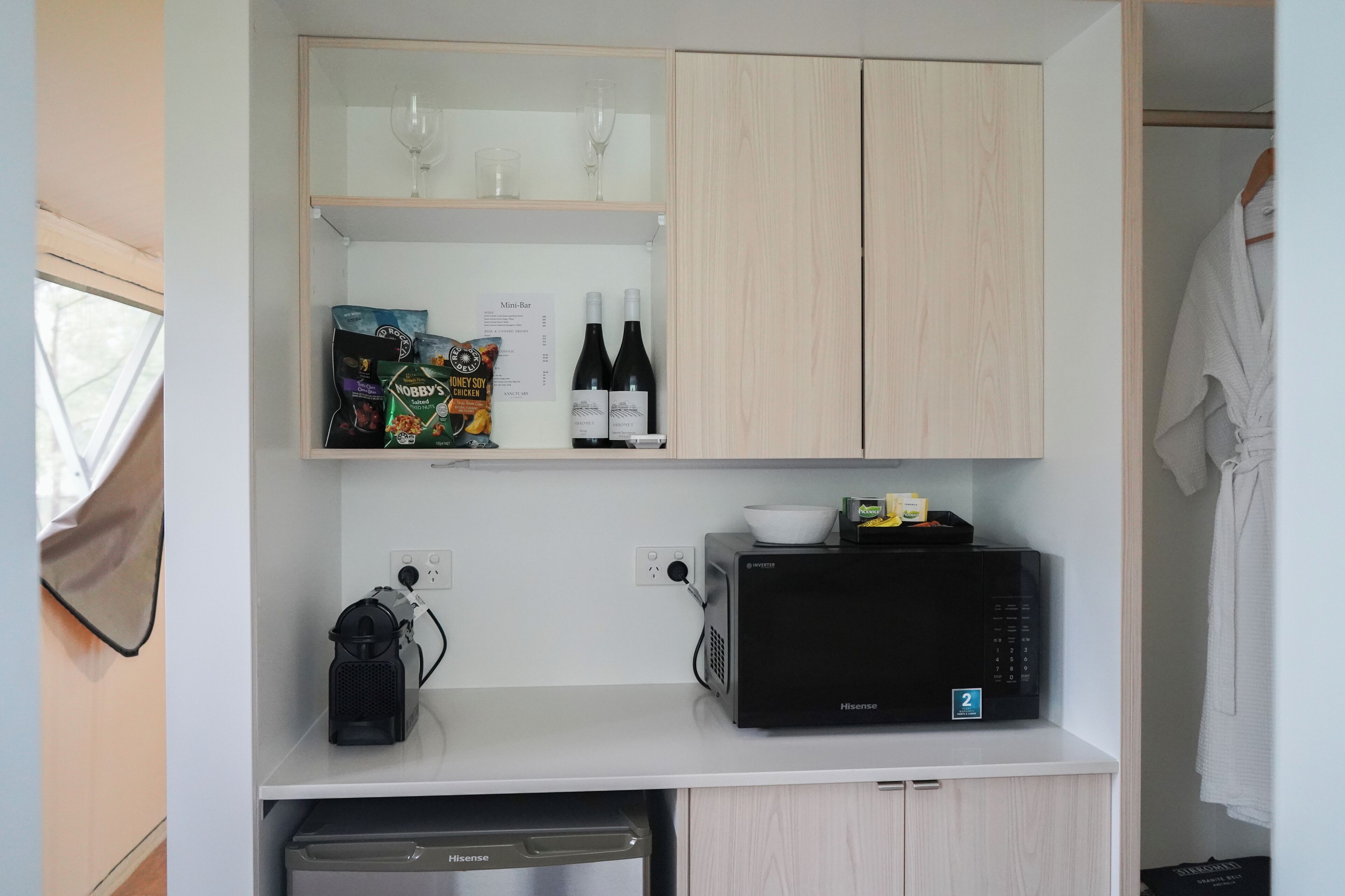 Uma cozinha compacta com micro-ondas, garrafas de vinho e cafeteira.