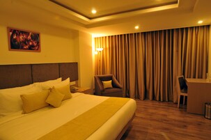 Quarto de hotel com uma cama grande, uma escrivaninha, uma cadeira e um quadro na parede.