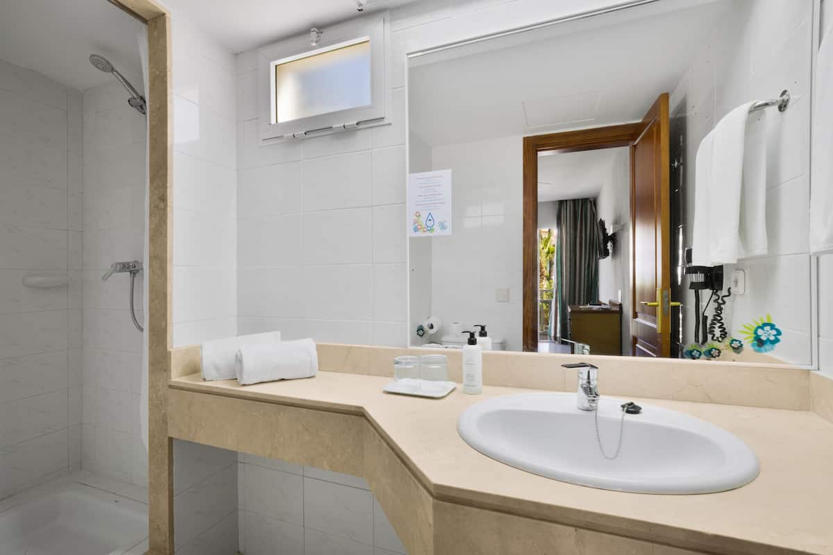 Uma casa de banho moderna com bancada bege, lavatório branco e chuveiro.